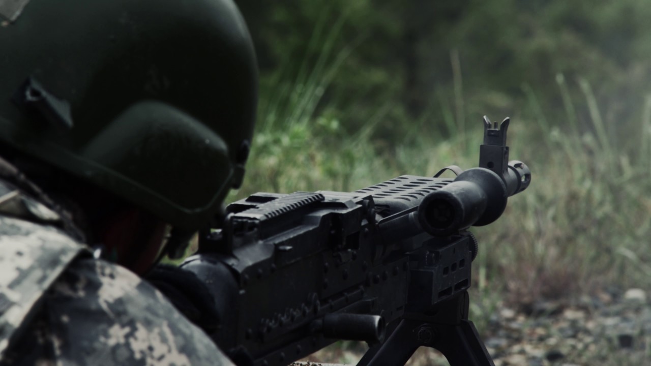 Close view over the shoulder of a soldier as he shoots a belt-fed ...