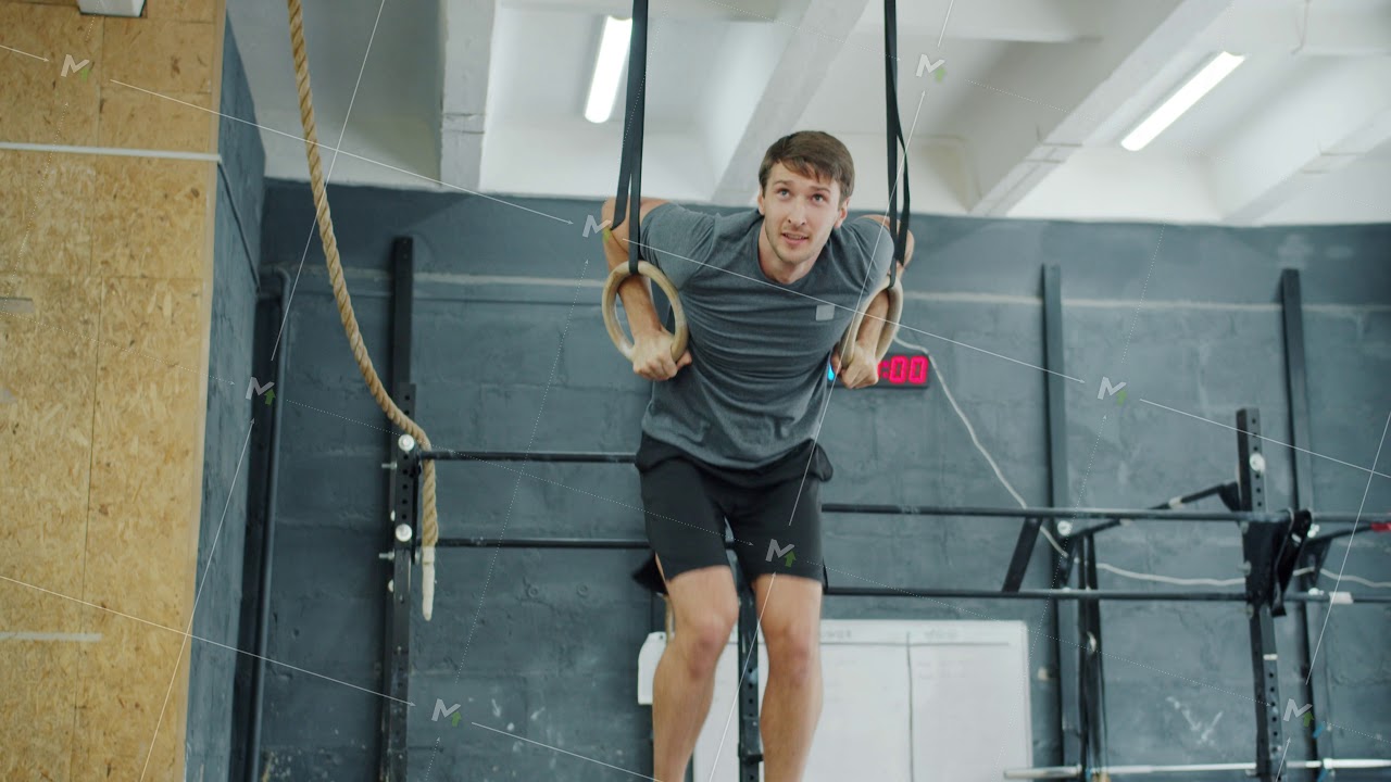 Young man doing exercises on still rings training in gym during ...