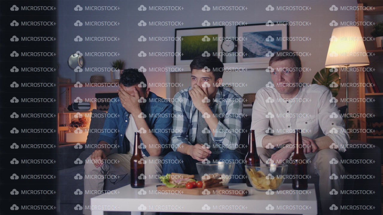 Unhappy young men with sad faces crying watching TV at night in ...