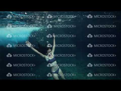 A young skinny woman in bikini floating underwater and holding her breath.