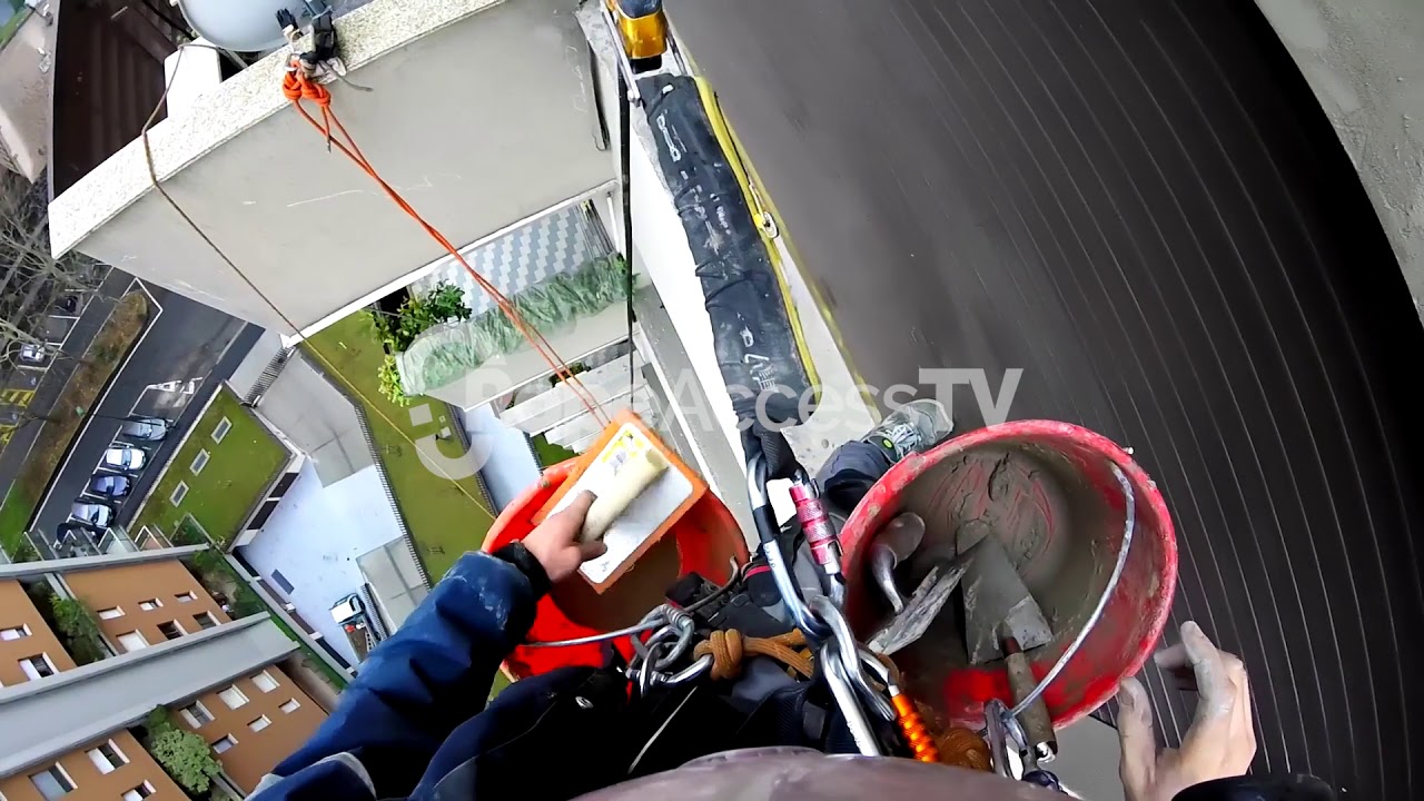 Abseiler working in construction use mortar to repair a damaged wall ...