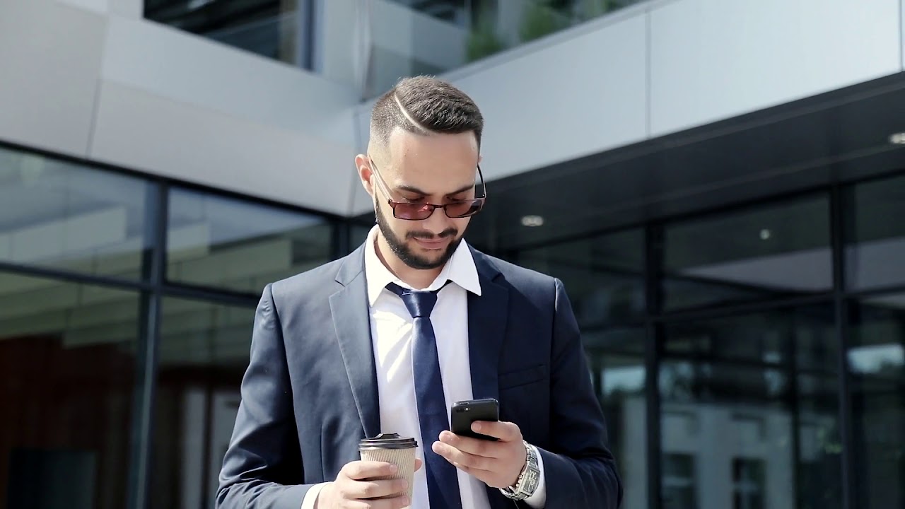 handsome stylish man exiting the modern office building drinking coffee ...