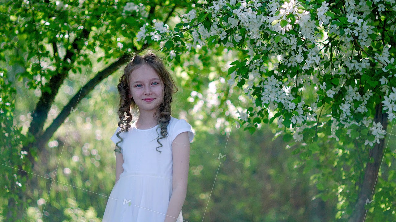 Smiling curly girl portrait in sunny garden on blooming fruit trees ...