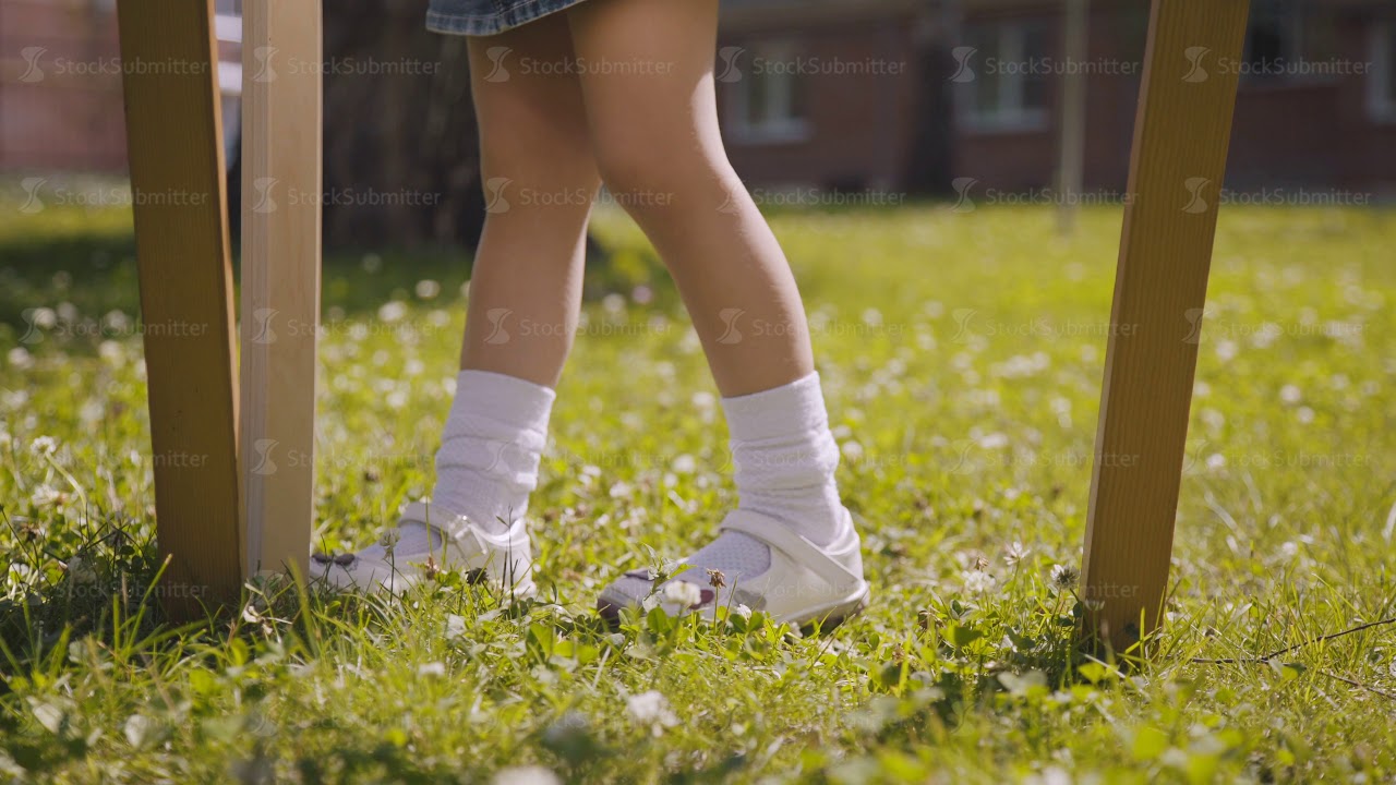 Children's legs girls stands on the grass and shifts from foot to foot ...