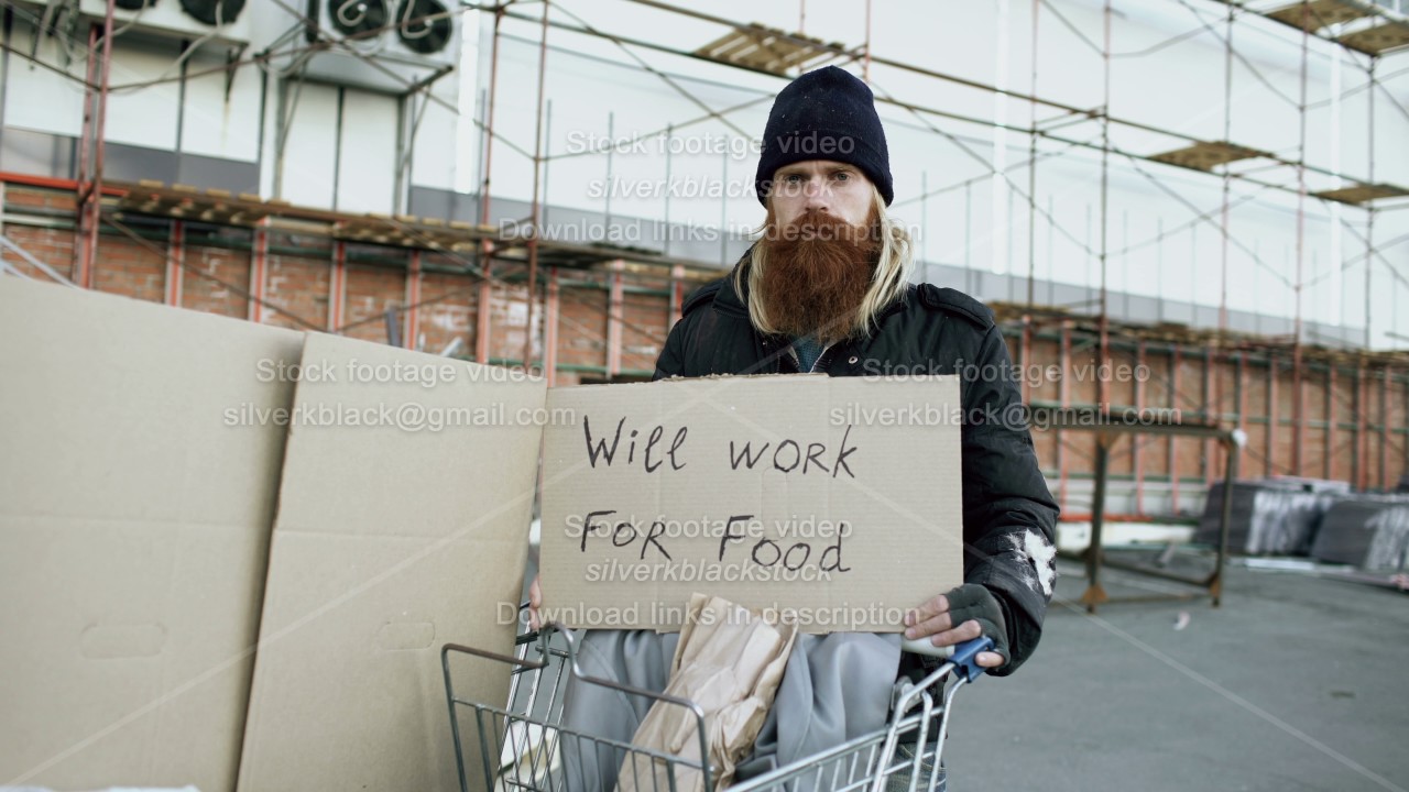Portrait of young homeless man with cardboard looking at camera and ...